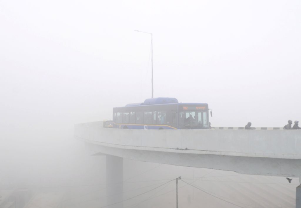 A bus makes a way on a bridge amid dense fog