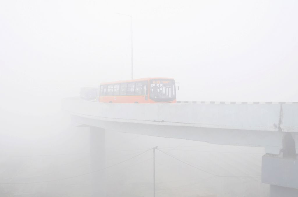 A bus makes a way on a bridge amid dense fog