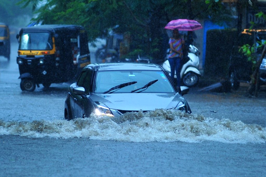 : Mumbai: A car half submerged wade through a waterlogged road