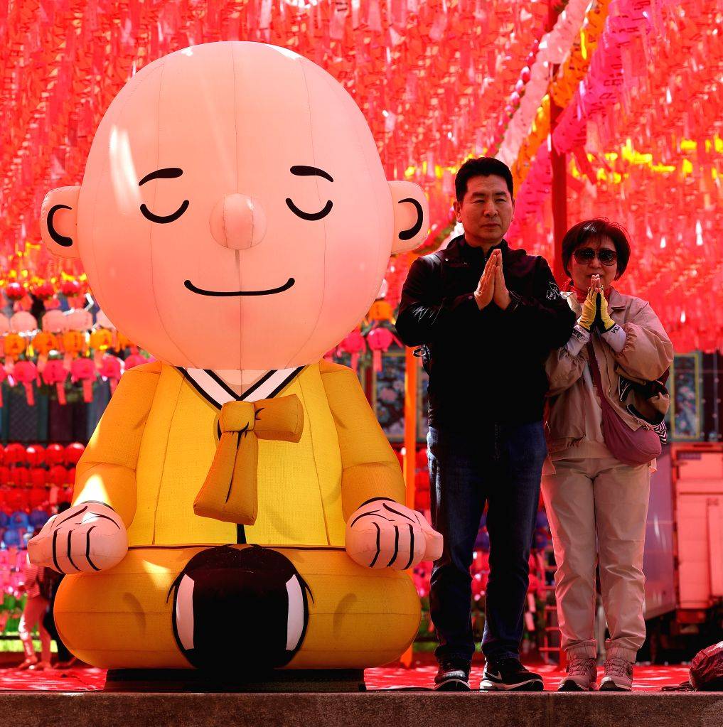 A couple, alongside a child monk installation, offers prayers under the ...