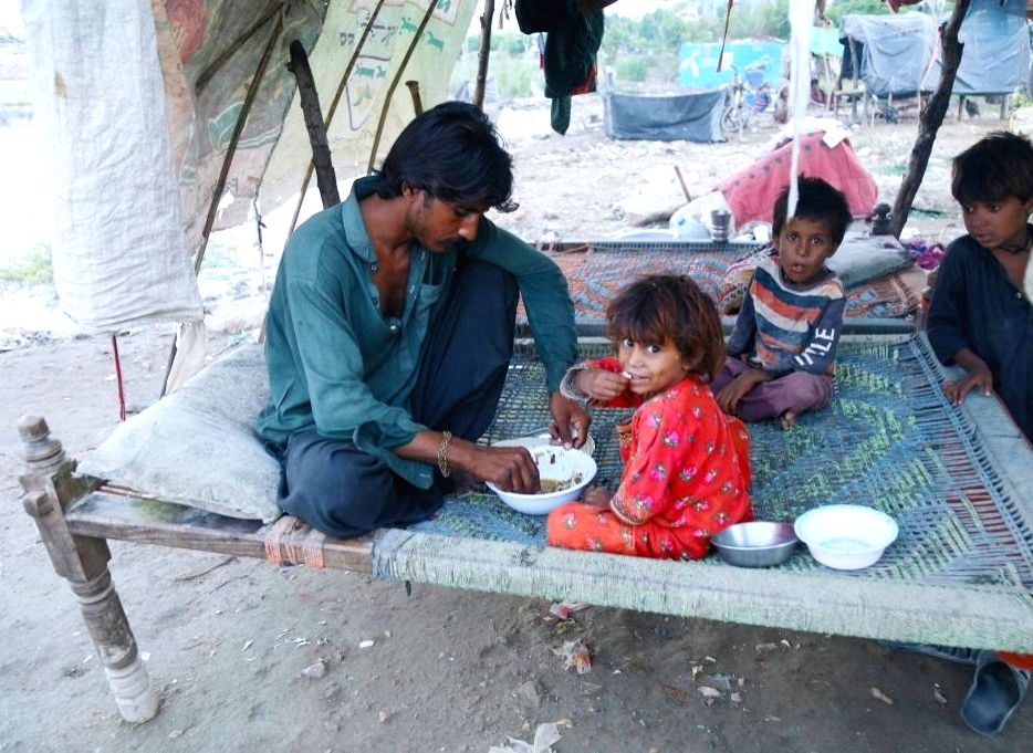 A flood-affected man with children eats food at a makeshift tent in ...