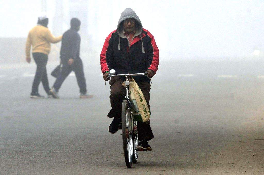 A man rides his bicycle amid dense fog on a cold winter morning