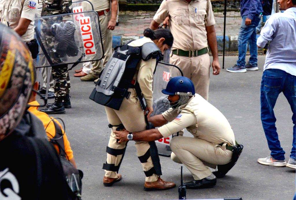A police officer helps a senior colleague put on a leg guard ahead of ...