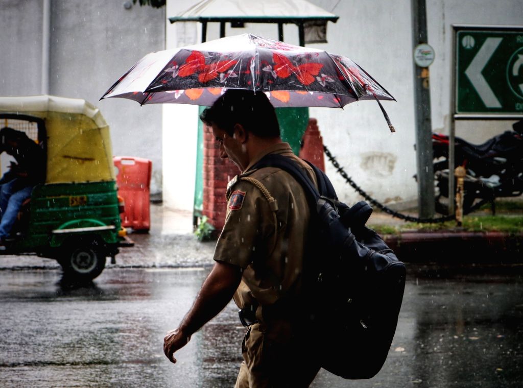 A police personnel holds an umbrella while walking past during rain