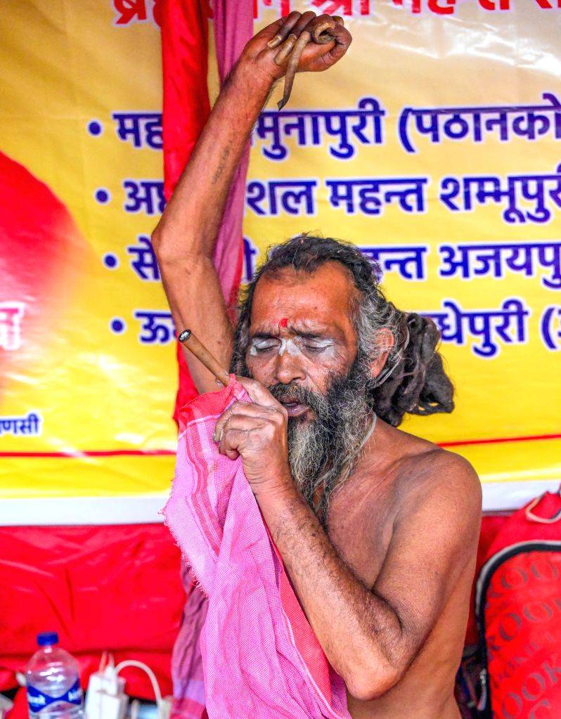 A Sadhu (Holy Man) with his hands raised in the air sitting at his camp
