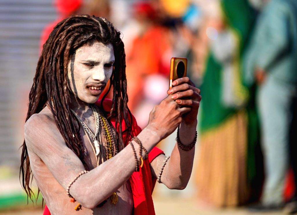 A sadhu takes a photograph with a mobile phone of newly initiated Naga ...