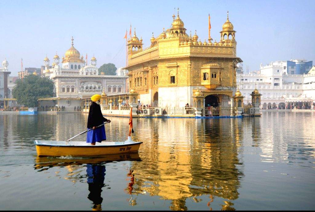 A Sikh Sewadar rows a boat at the holy sarovar with the backdrop of the ...