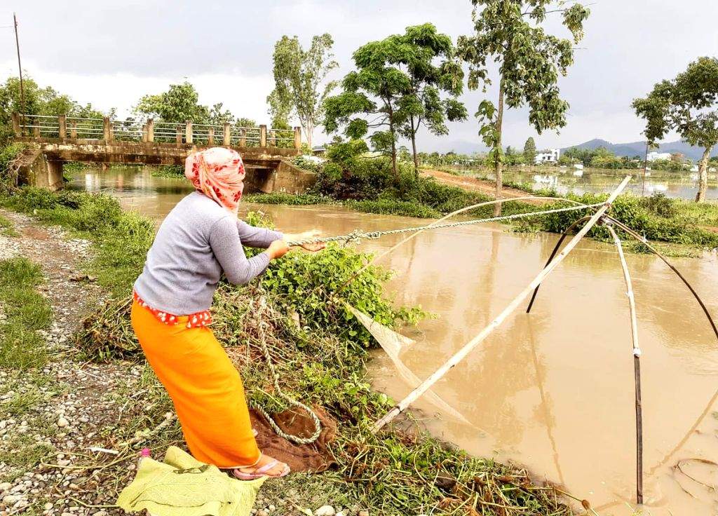 A woman throws a fishing net into an overflowing stream following ...