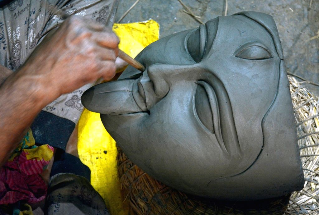 An artist gives finishing touches to a clay face of Goddess Kali's idol