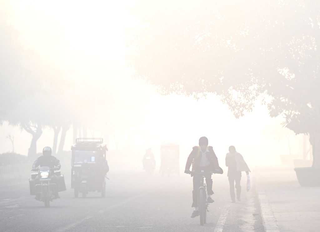 Commuters walk along a road amid smog on a chilly morning