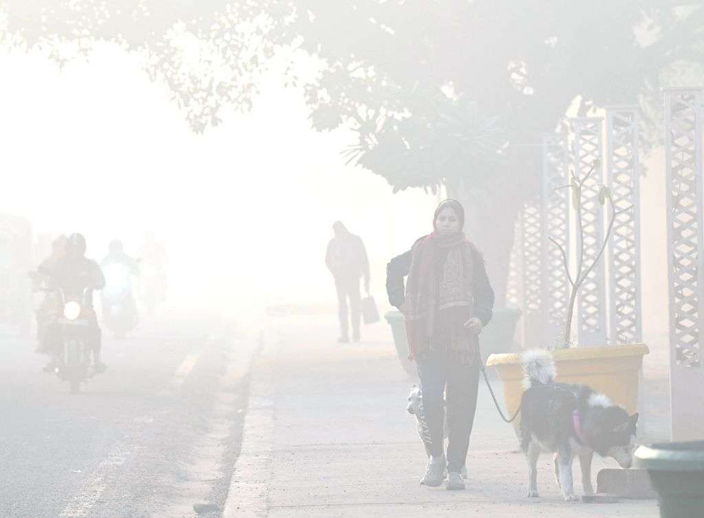 Commuters walk along a road amid smog on a chilly morning