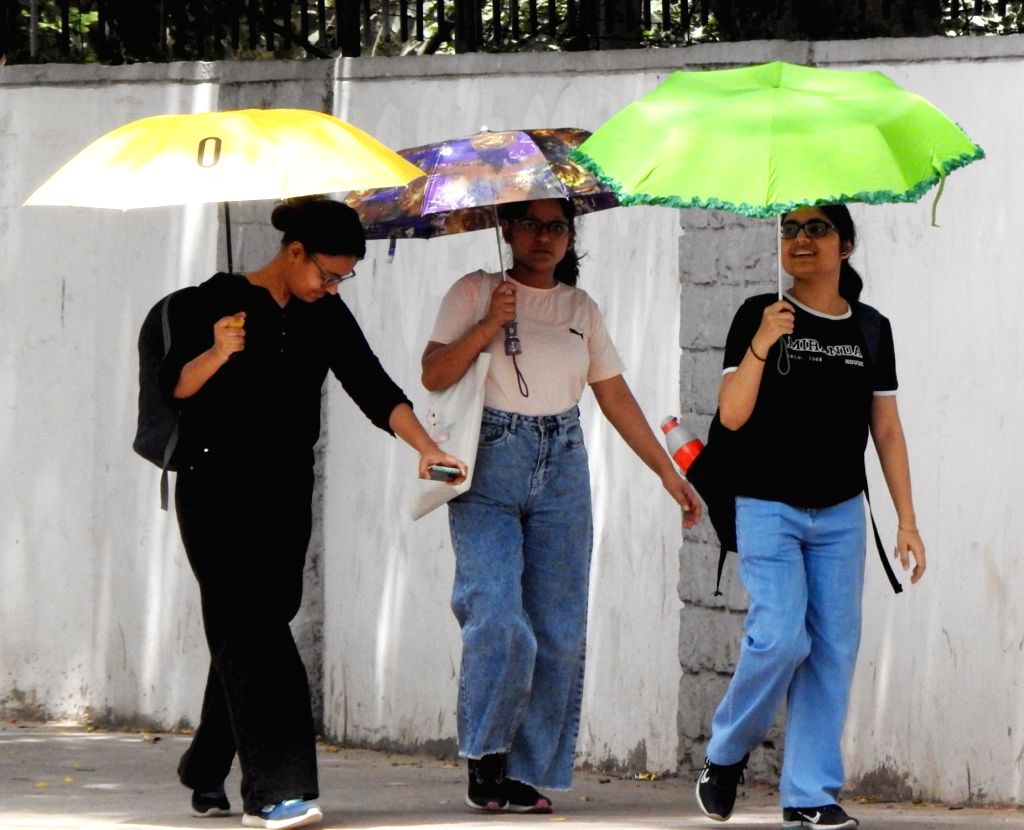 New Delhi : Commuters walk under the shade of umbrellas to protect ...