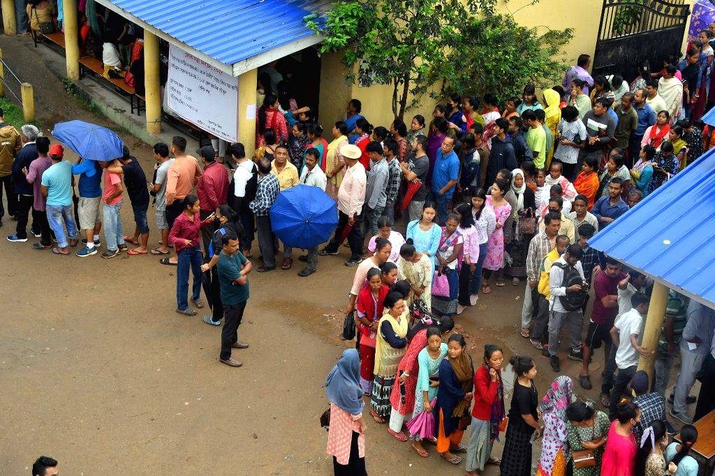 People wait in queues to cast their votes amid rains at a polling ...