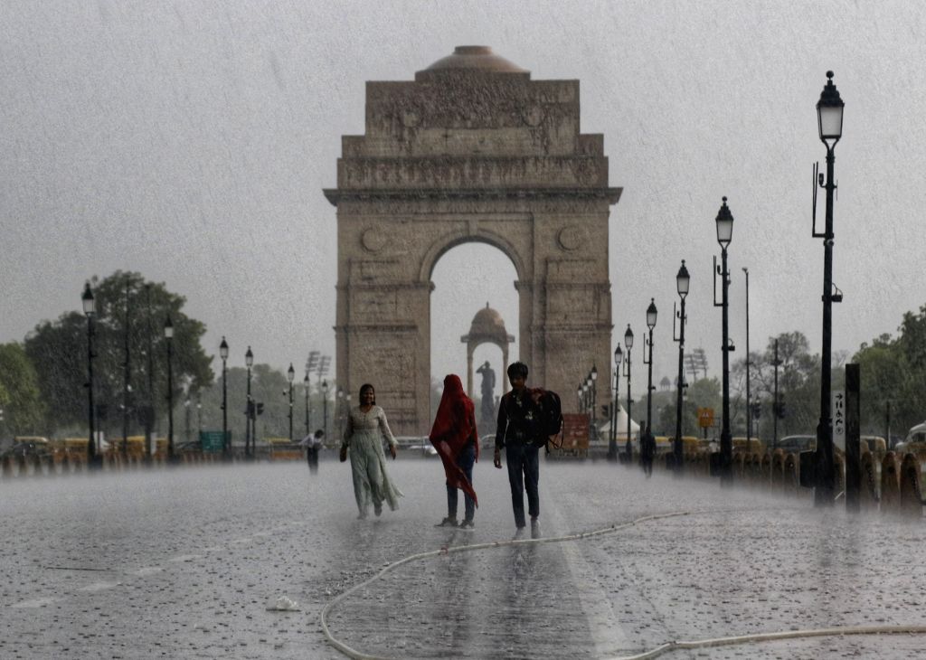 People walk past amid rain at India Gate