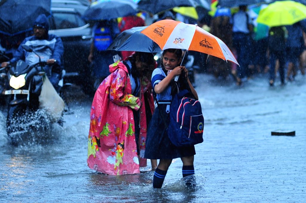: Mumbai: School students hold umbrellas wade through a waterlogged road