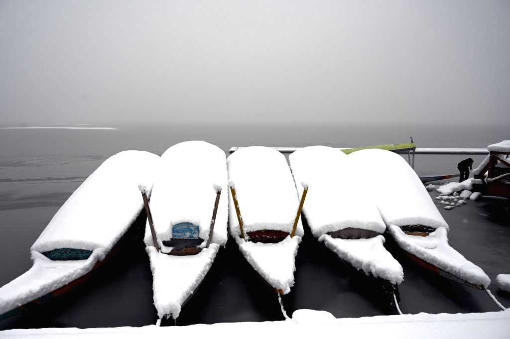 Snow-covered boats anchored at the corner of the frozen Dal Lake after ...